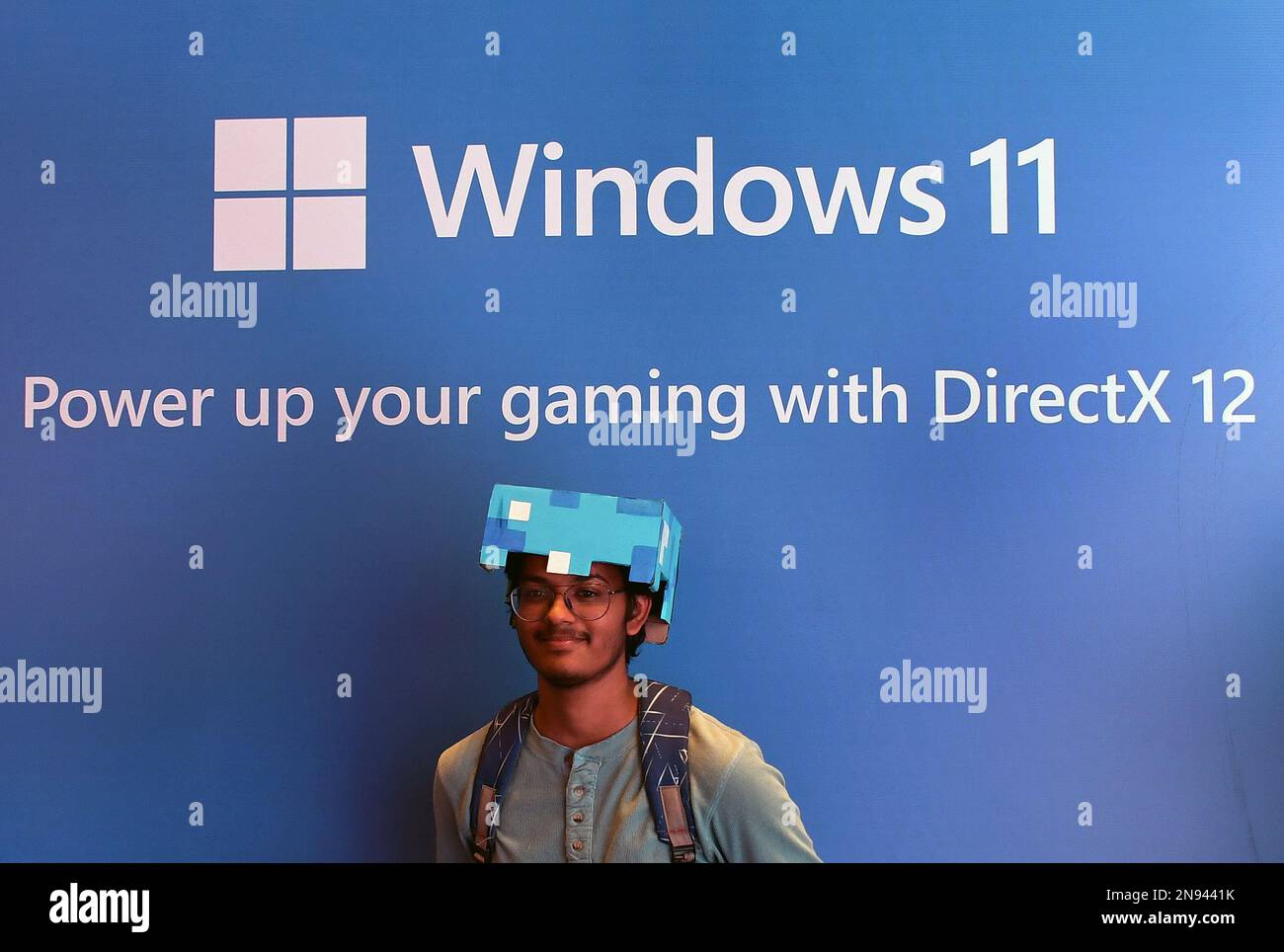 A boy poses for a photo below Windows 11 poster at Comic Con event. The ...