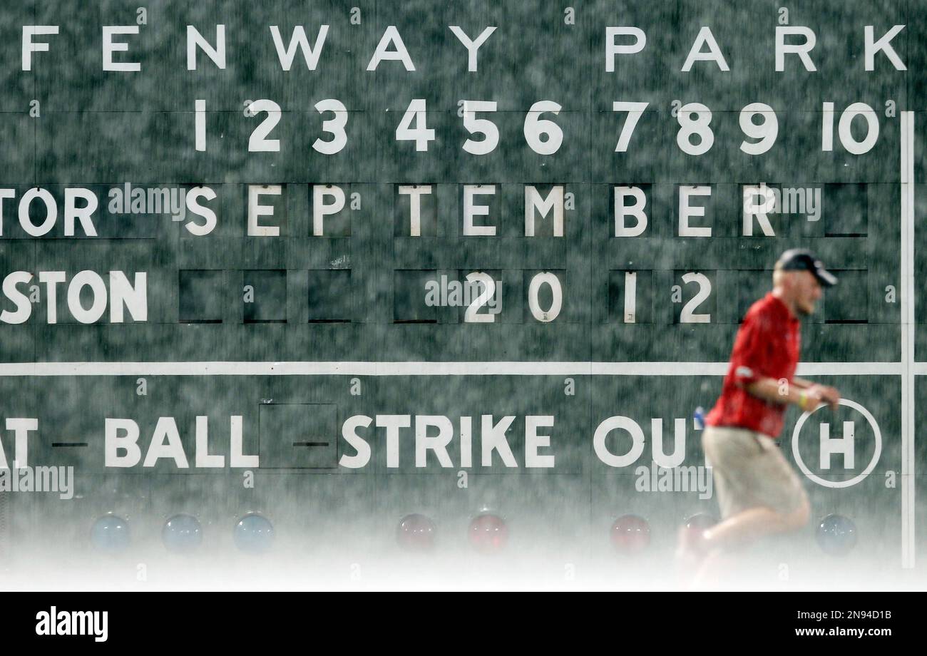 A member of the Fenway Park grounds crew runs through heavy rain before ...