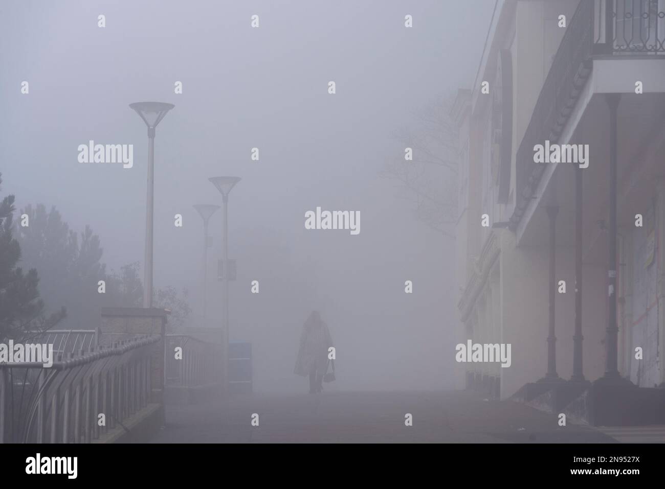 Female walking up pier hill shrouded in fog alone, disappearing into ...