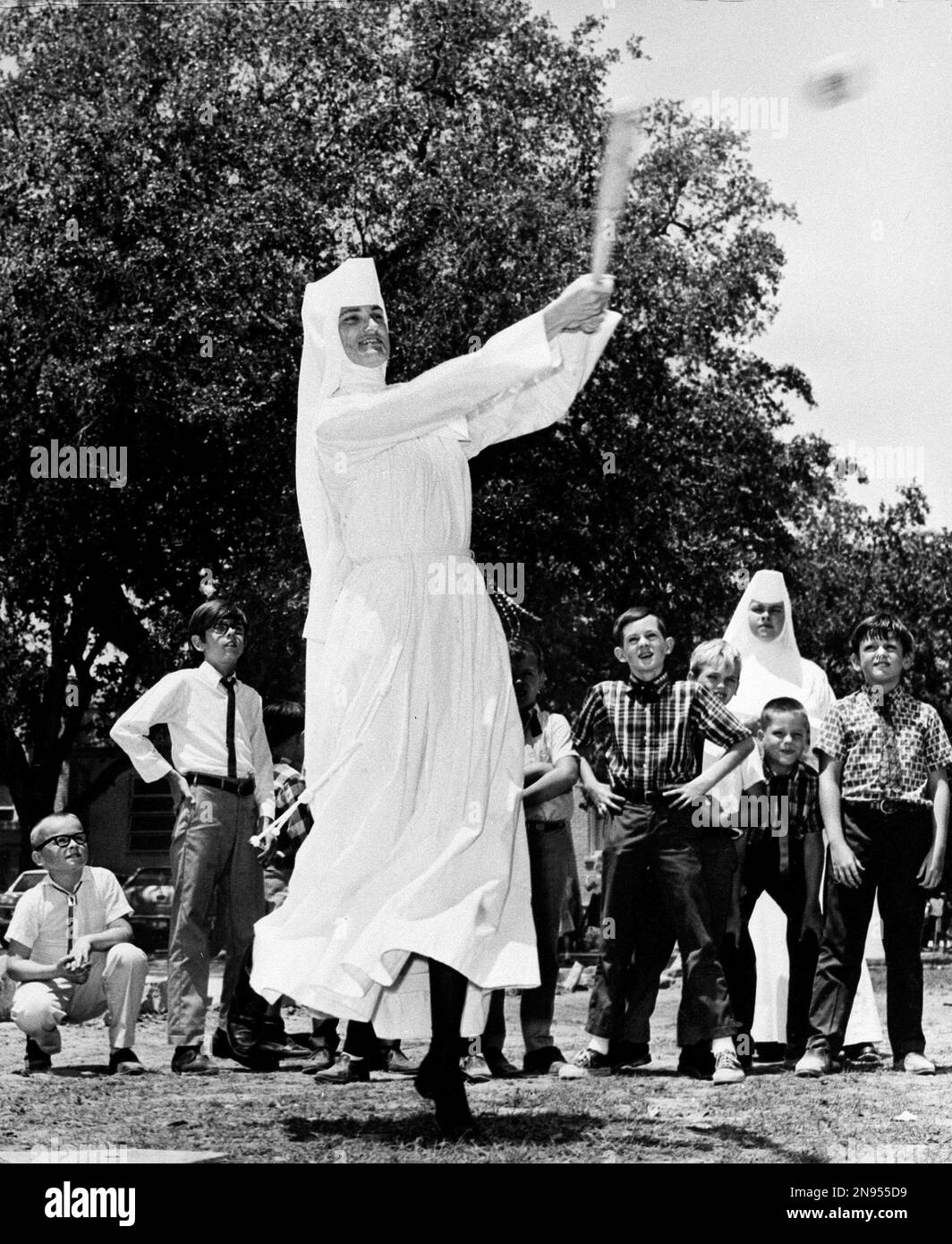 A nun is shown swinging a bat during a softball game, date and location ...
