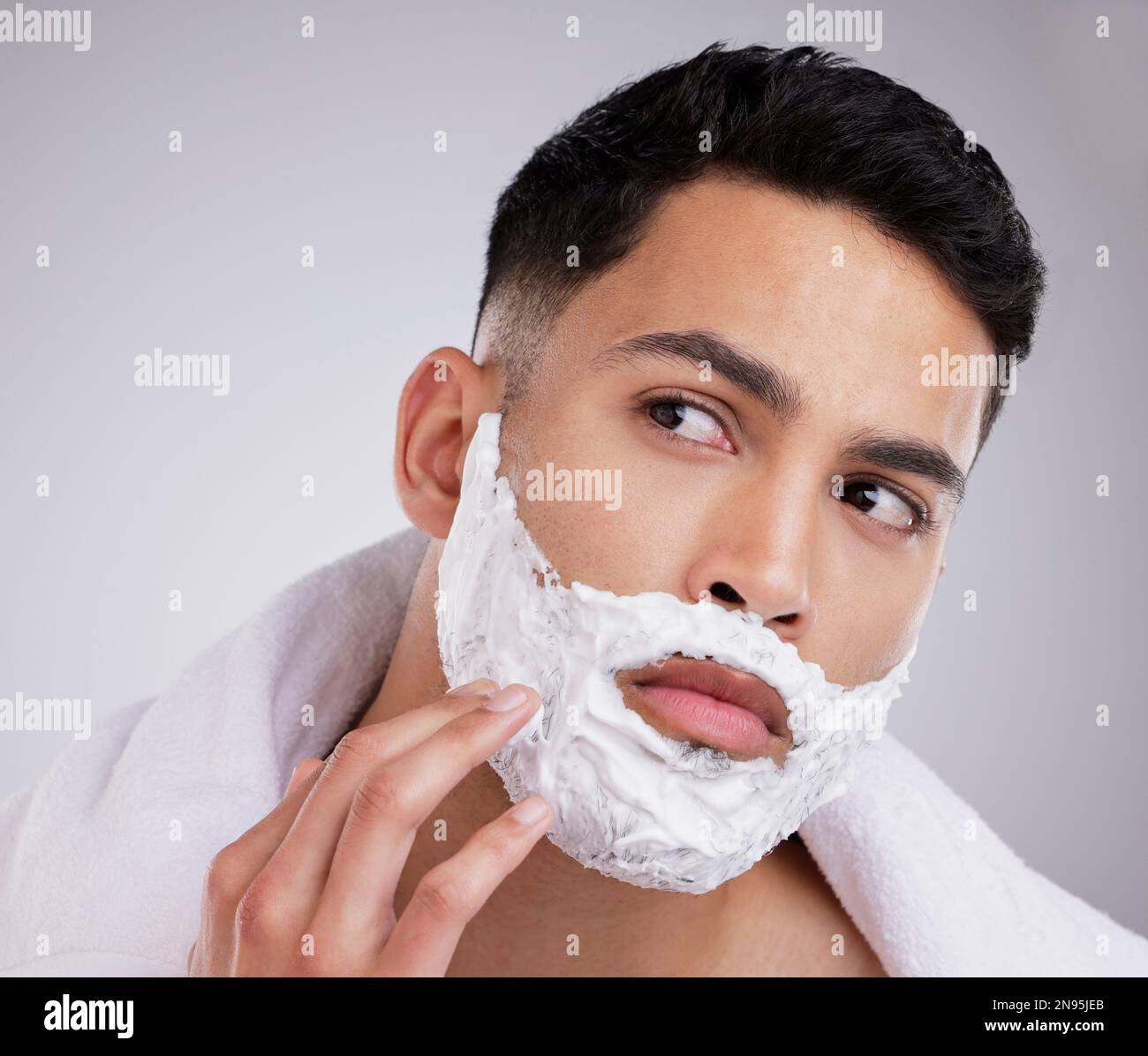 A shaven face appears youthful. a young man applying shaving cream to his face against a studio ...