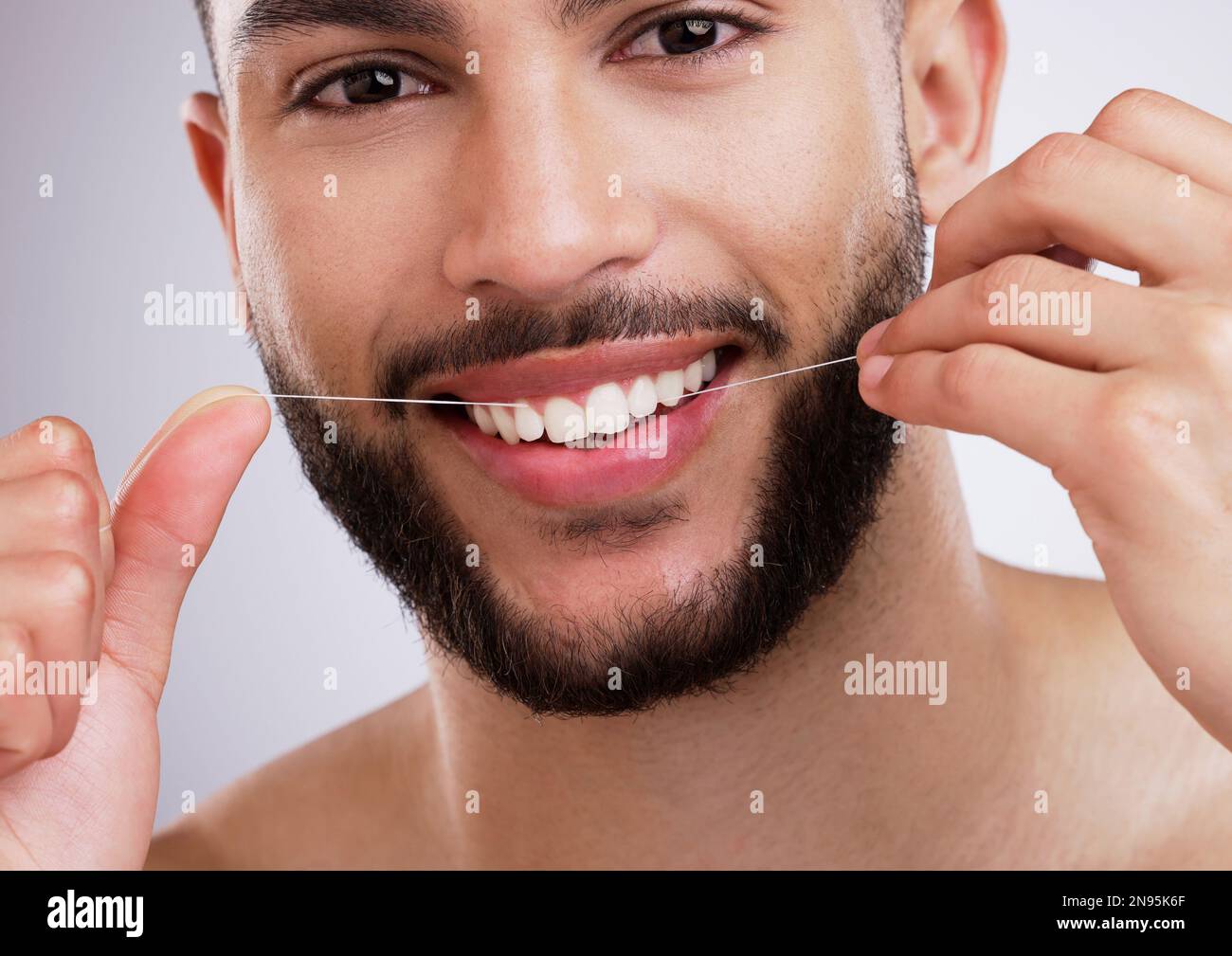 Twice a day keeps them in tip top shape. a young man flossing his teeth against a studio ...