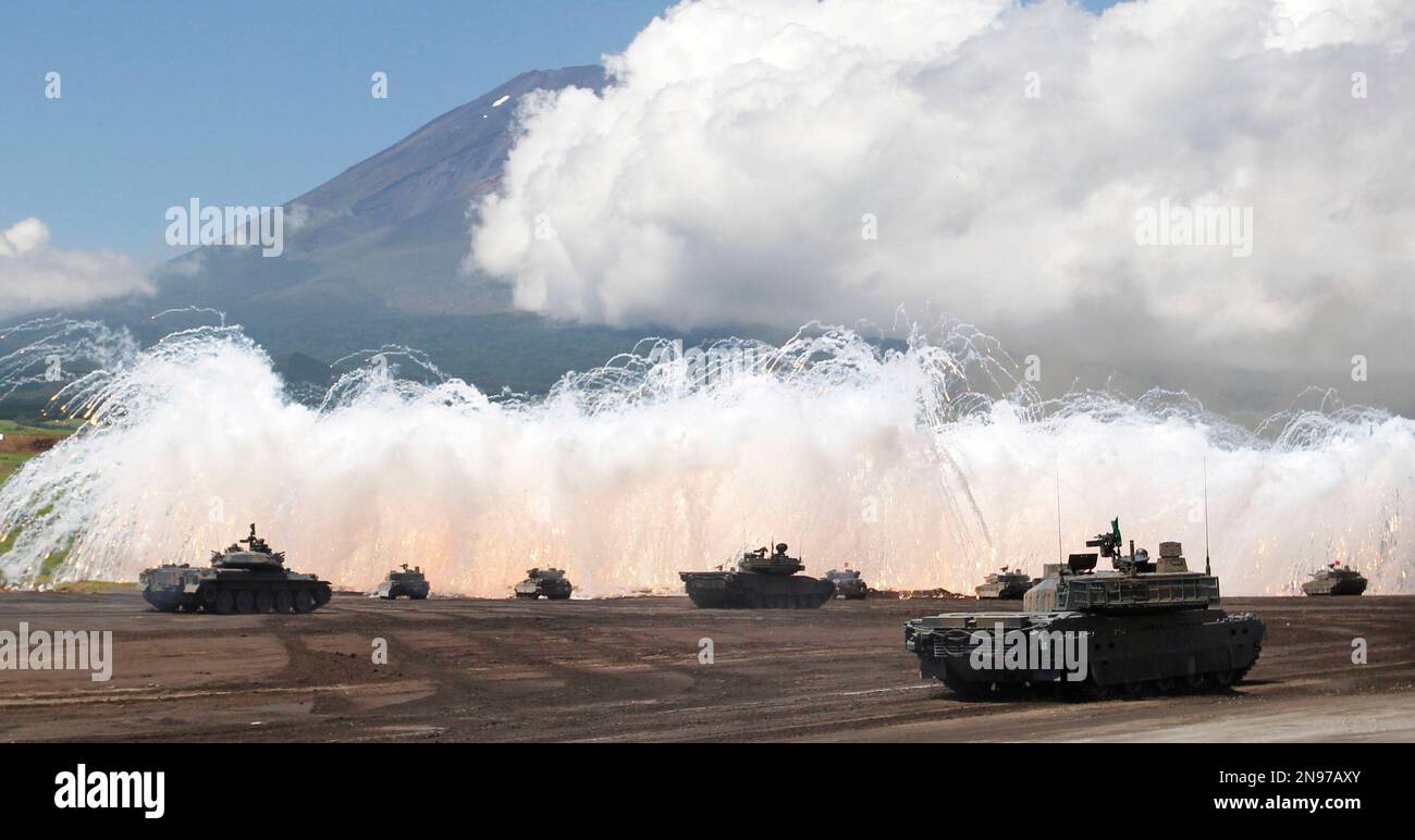 A line of Japan Ground Self-Defense Force tanks flare up a smoke screen ...