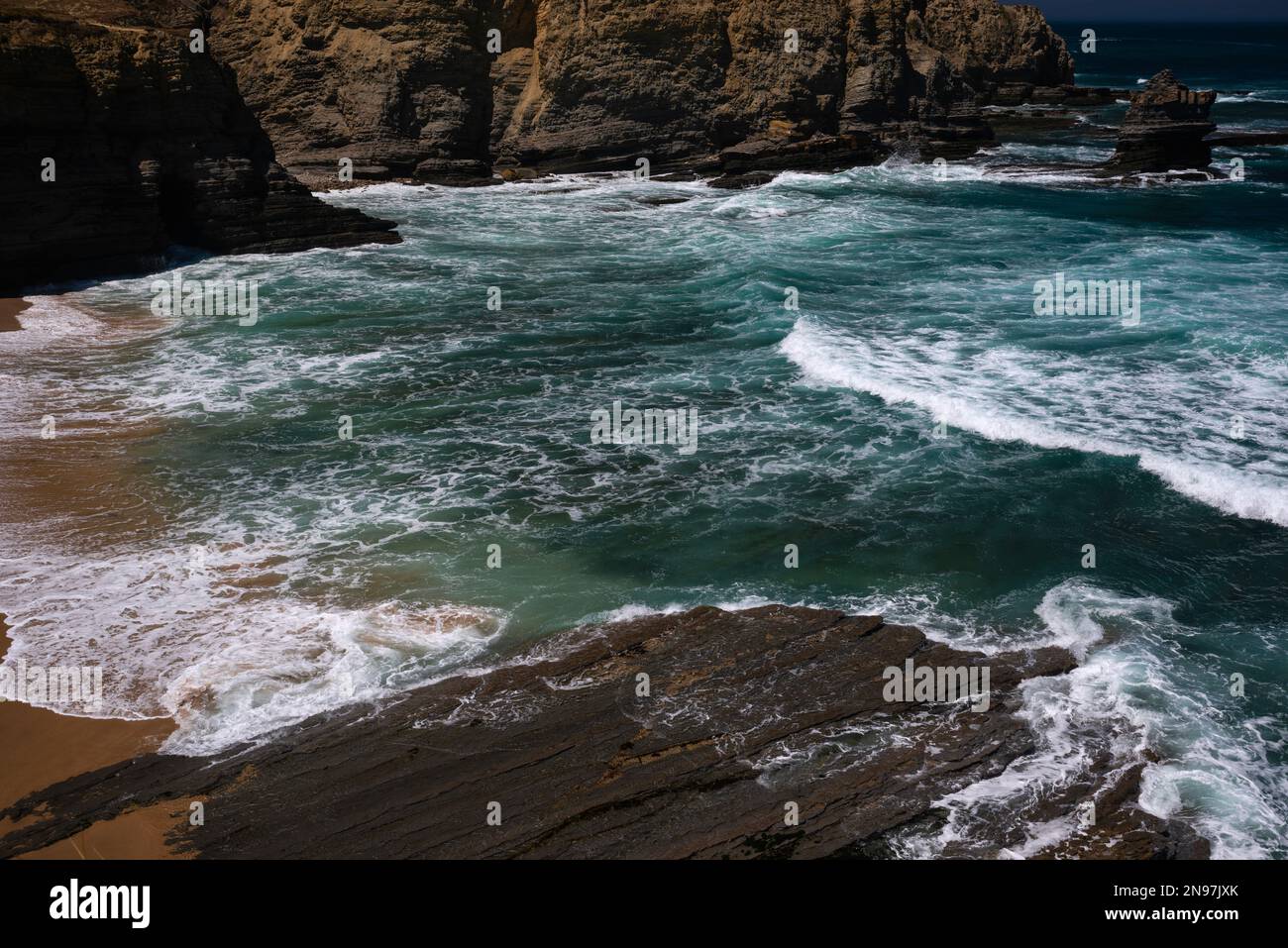 White surf on green Atlantic waves surging up a shelving sandy beach ...