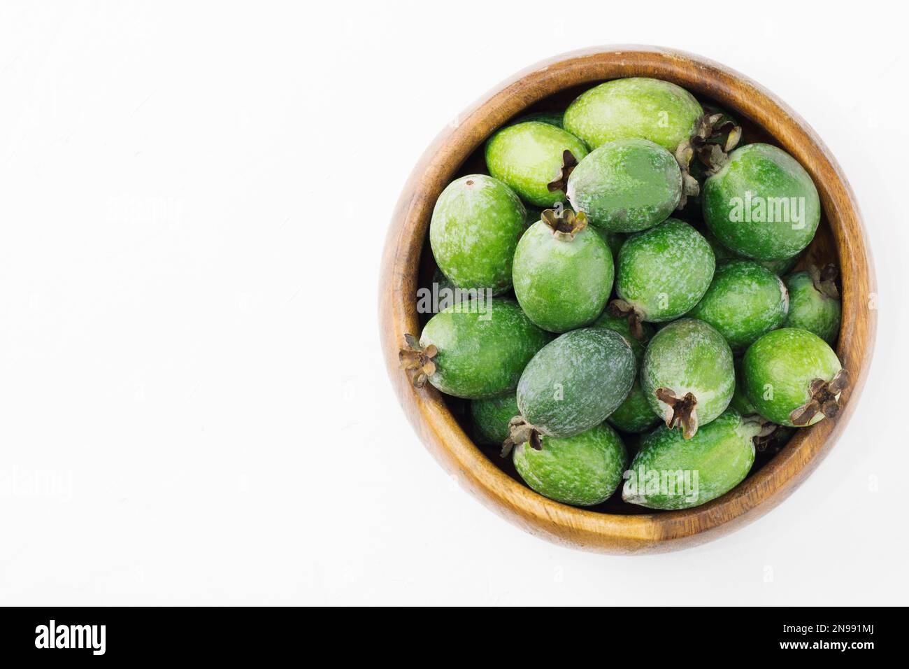 Green feijoa fruits in a wooden plate on a white background. Tropical ...