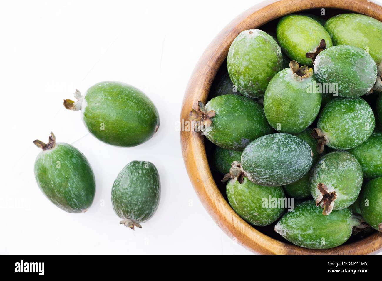 Green feijoa fruits in a wooden plate on a white background. Tropical fruit feijoa. Set of ripe ...