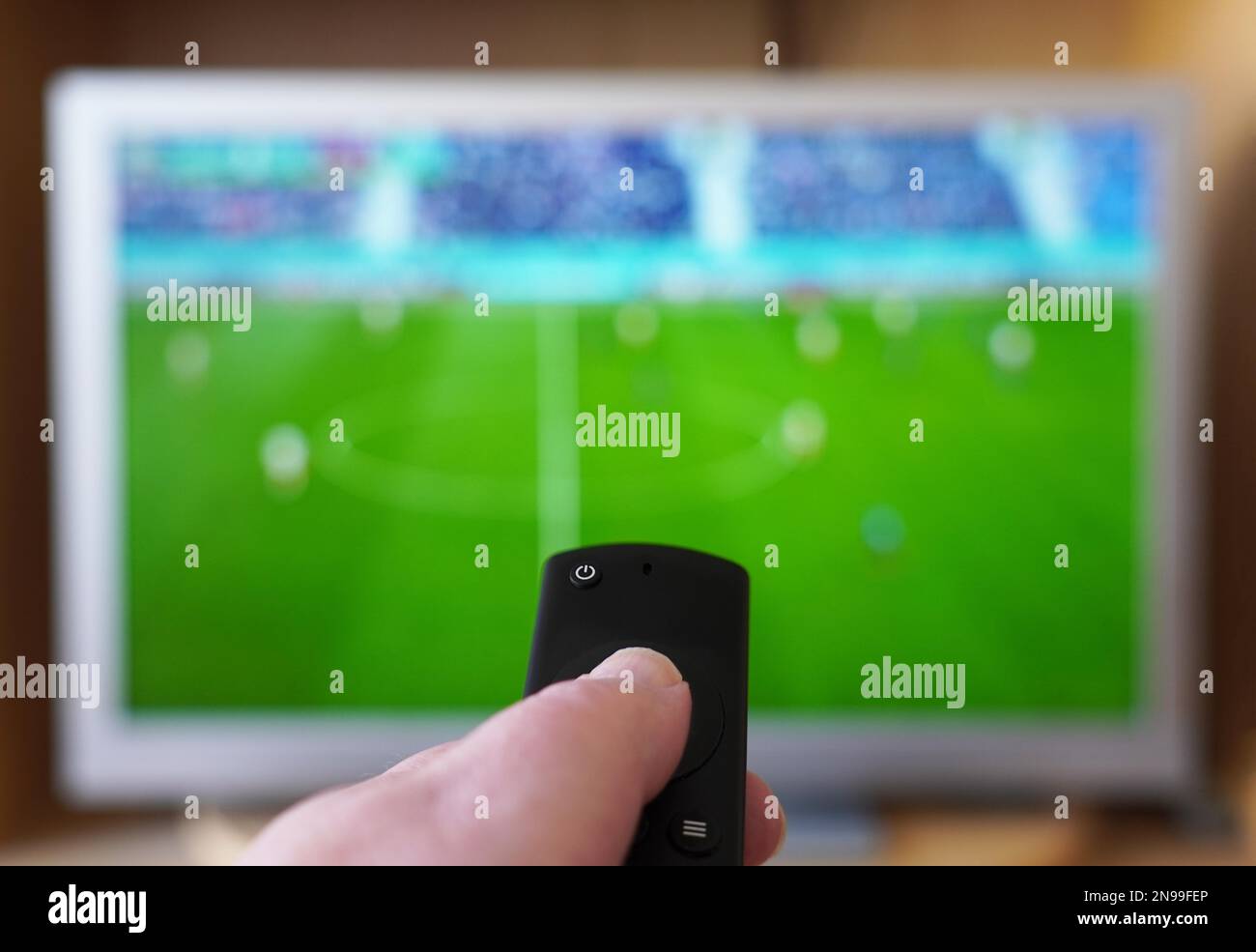 hand pointing remote control at tv set with soccer or football match ...