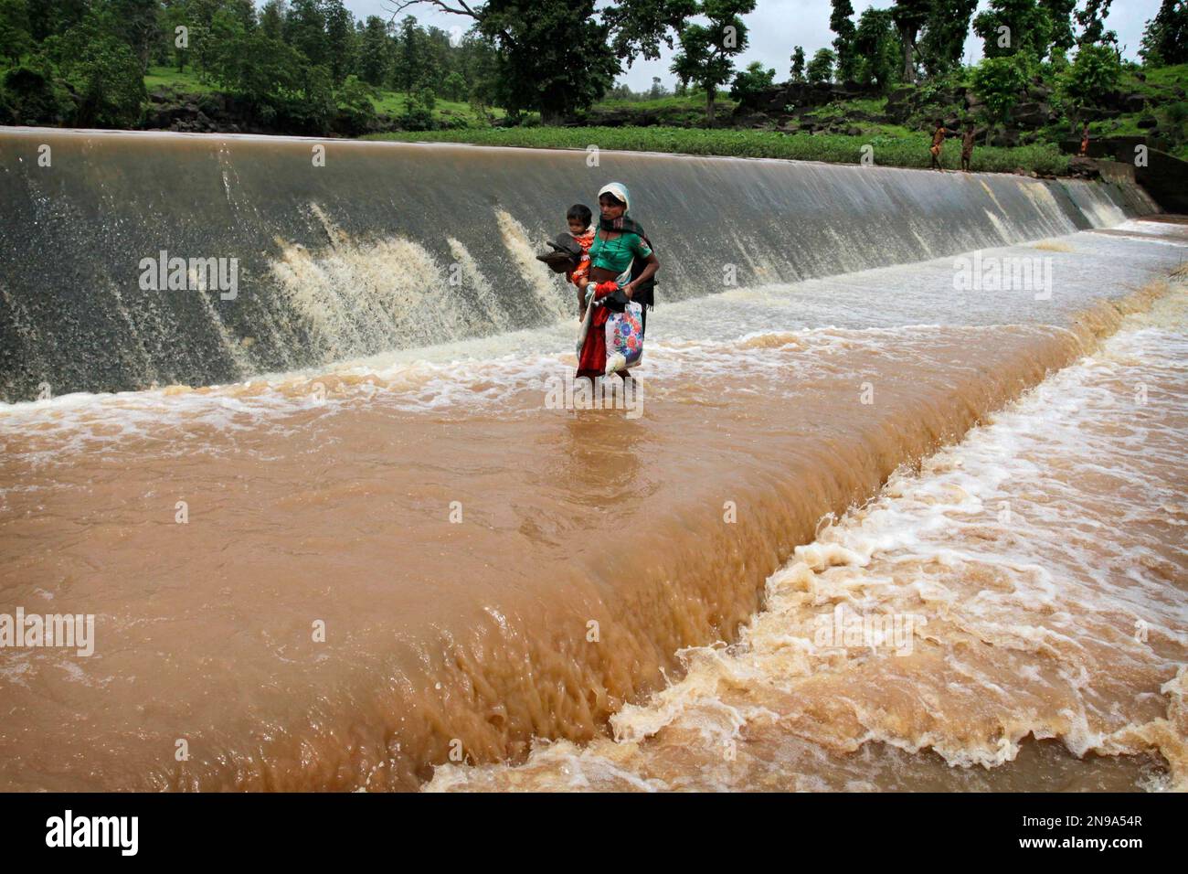 An Indian tribal woman carries her child as she crosses water from ...
