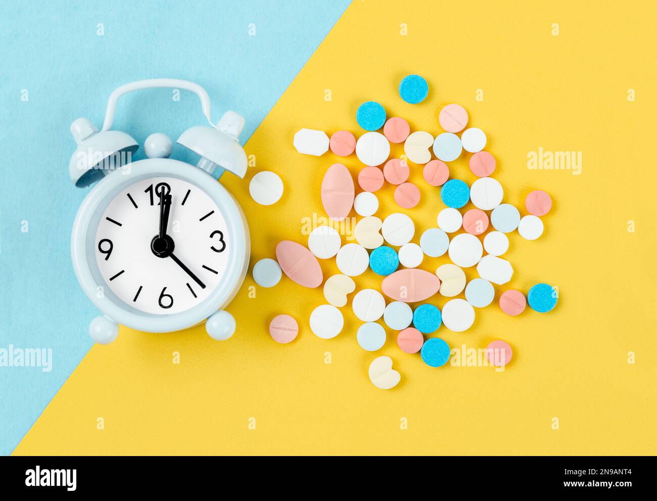 White alarm clock and many drug on a yellow background. Taking medicine ...