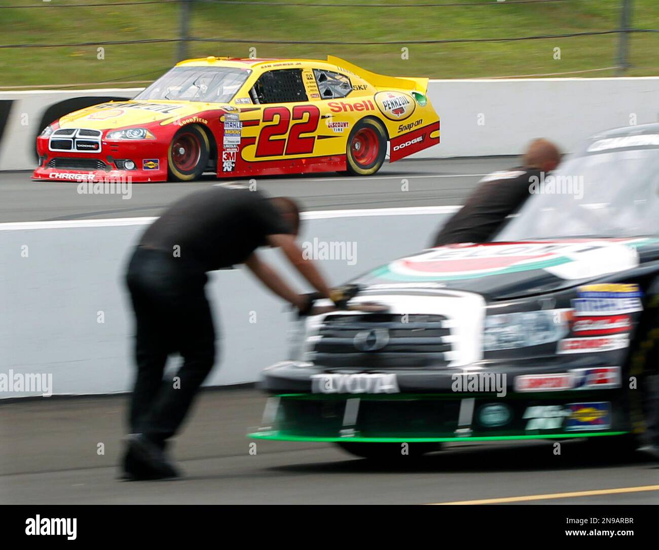 As a crew pushes a race truck in the pits, Sam Hornish Jr. (22) races ...