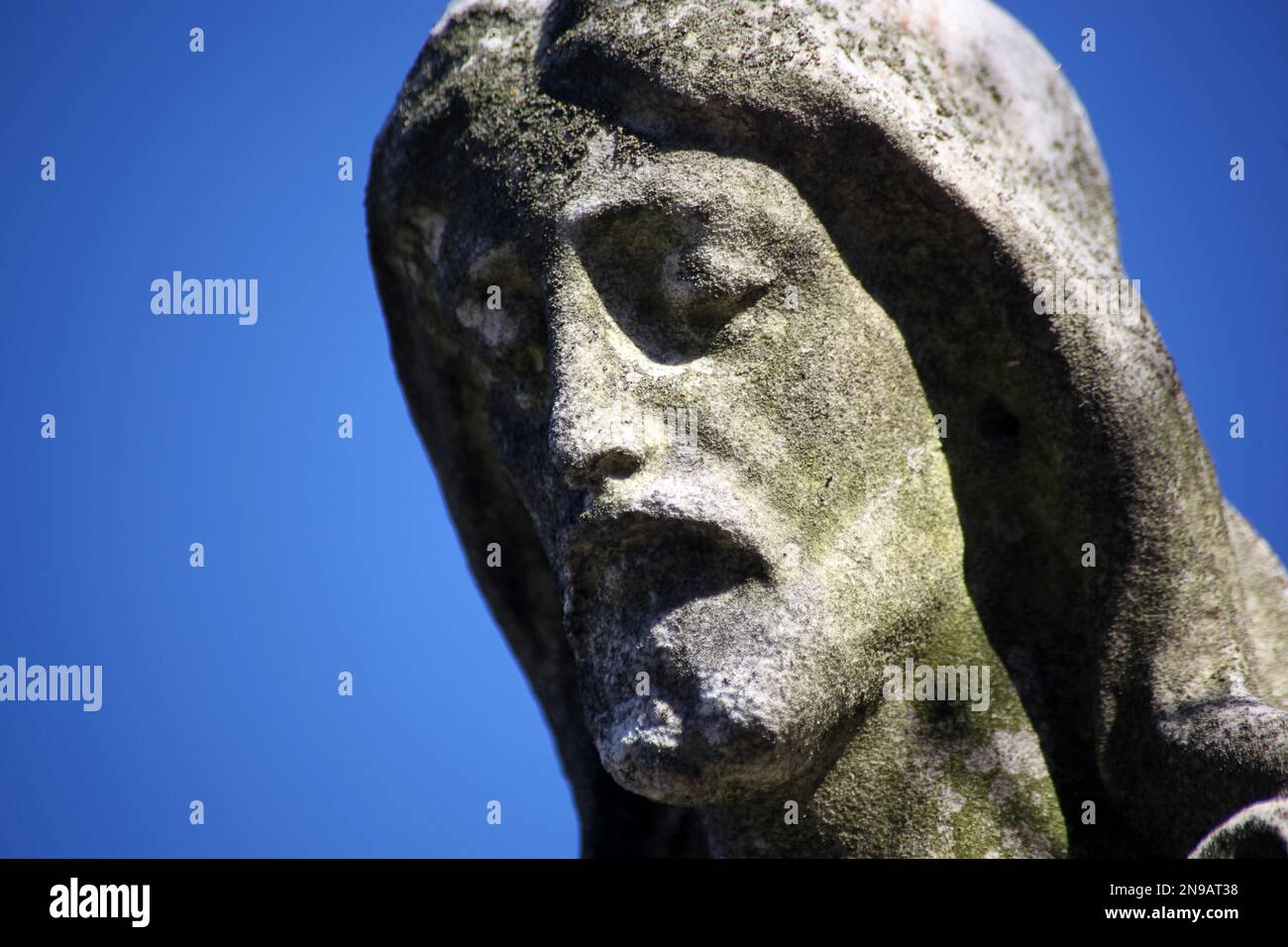 Close up face of Jesus Christ crumbling moss covered stone graveyard statue. Selective focus ...