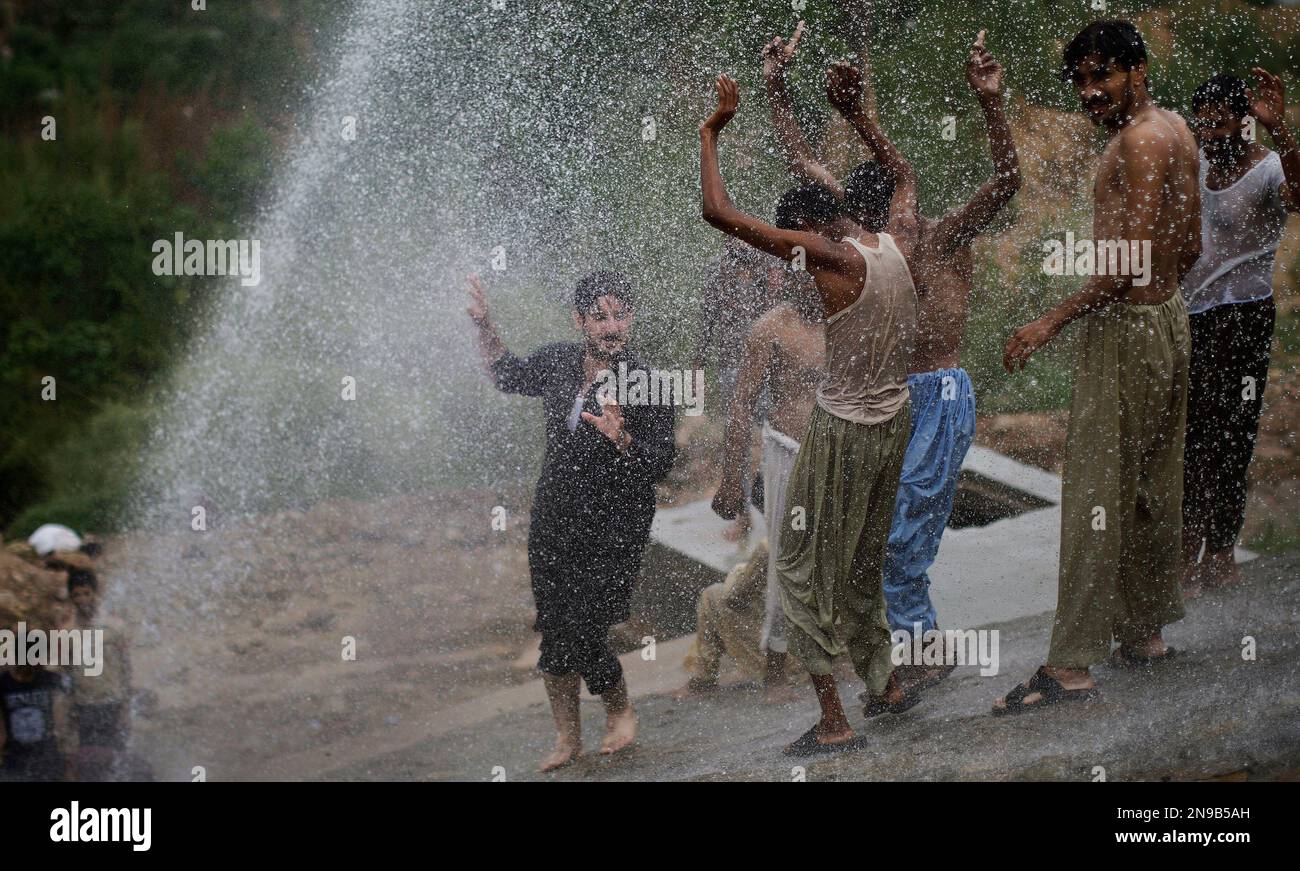 Pakistani men react while cooling off under water splashed from a ...