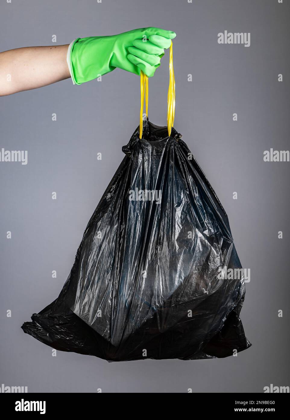 Hand in glove holding handles of black plastic disposable trash bag ...