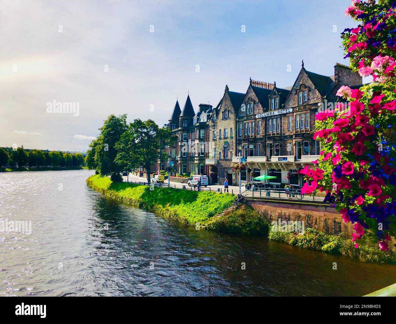 The view of riverside buildings with flowers and green trees. Inverness ...