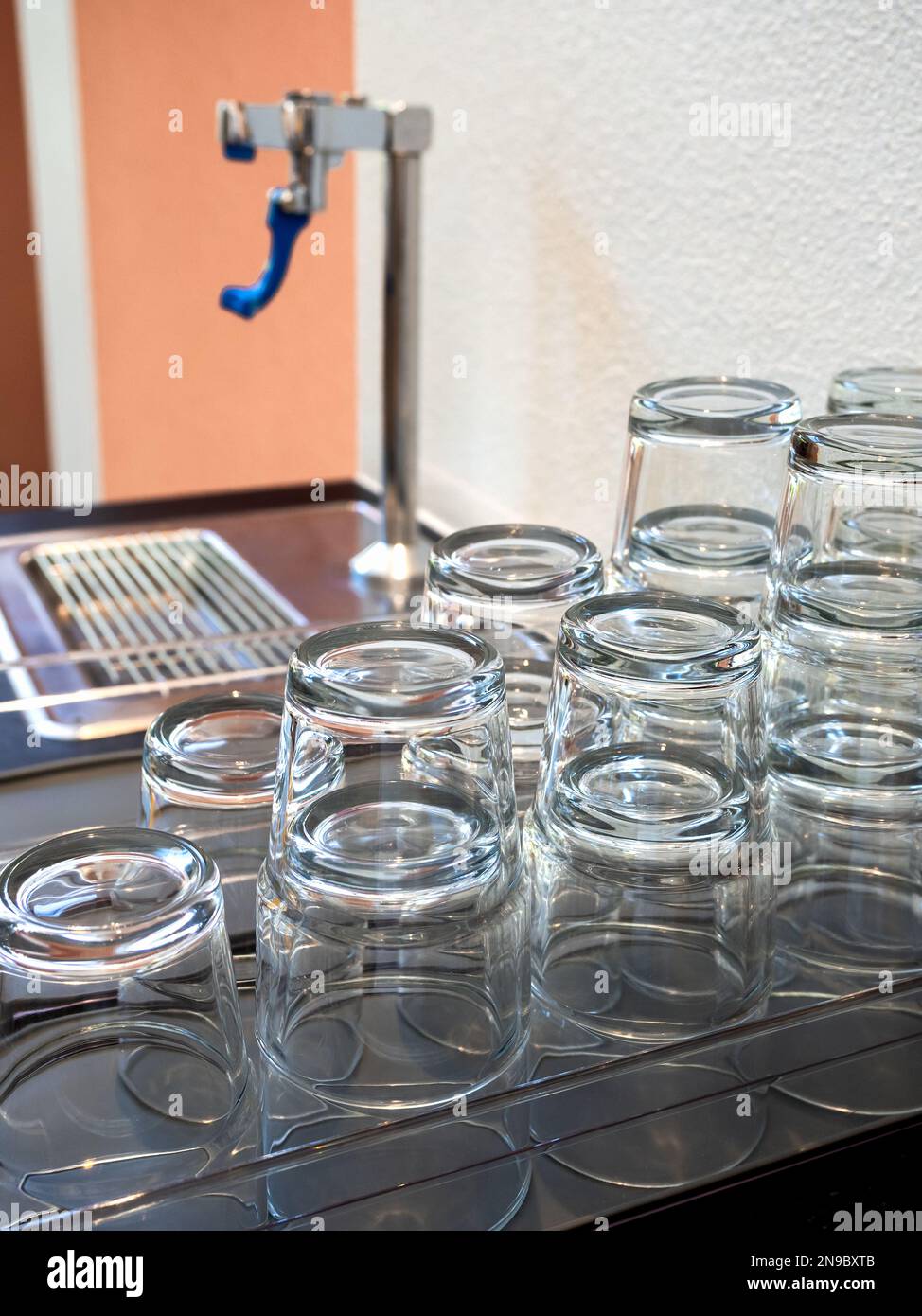 Stacks of clean empty glasses on stainless cooler water near the faucet ...