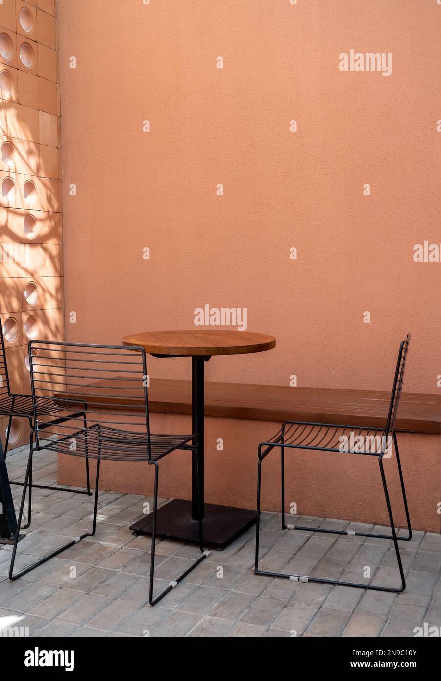 Three empty black wire chairs, long bench seat and round wooden table ...