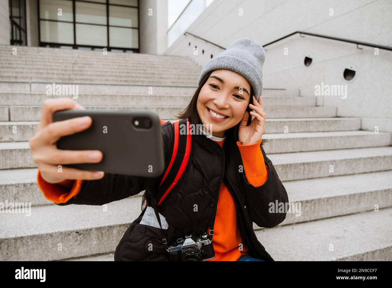 Beautiful young smiling asian woman in warm clothes taking selfie while ...