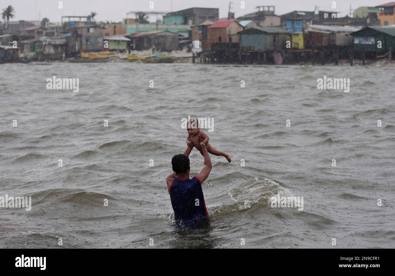 A Filipino man plays with his son as they swim despite rain and waves ...