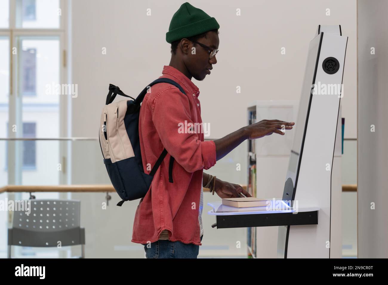 Young African student guy standing in library using self-service ...