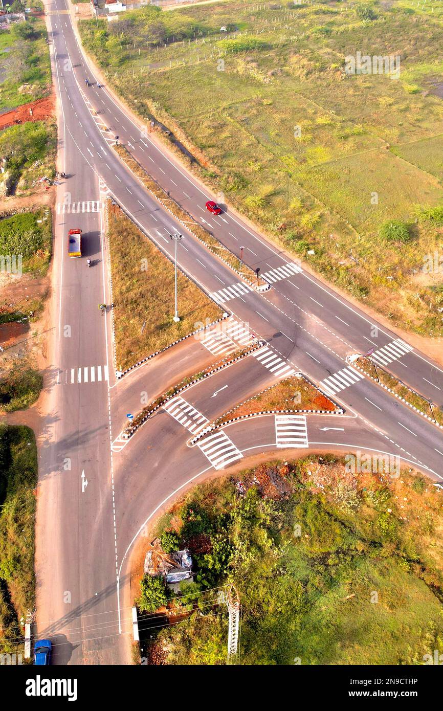 A vertical drone shot of cars on an asphalt road surrounded by green ...