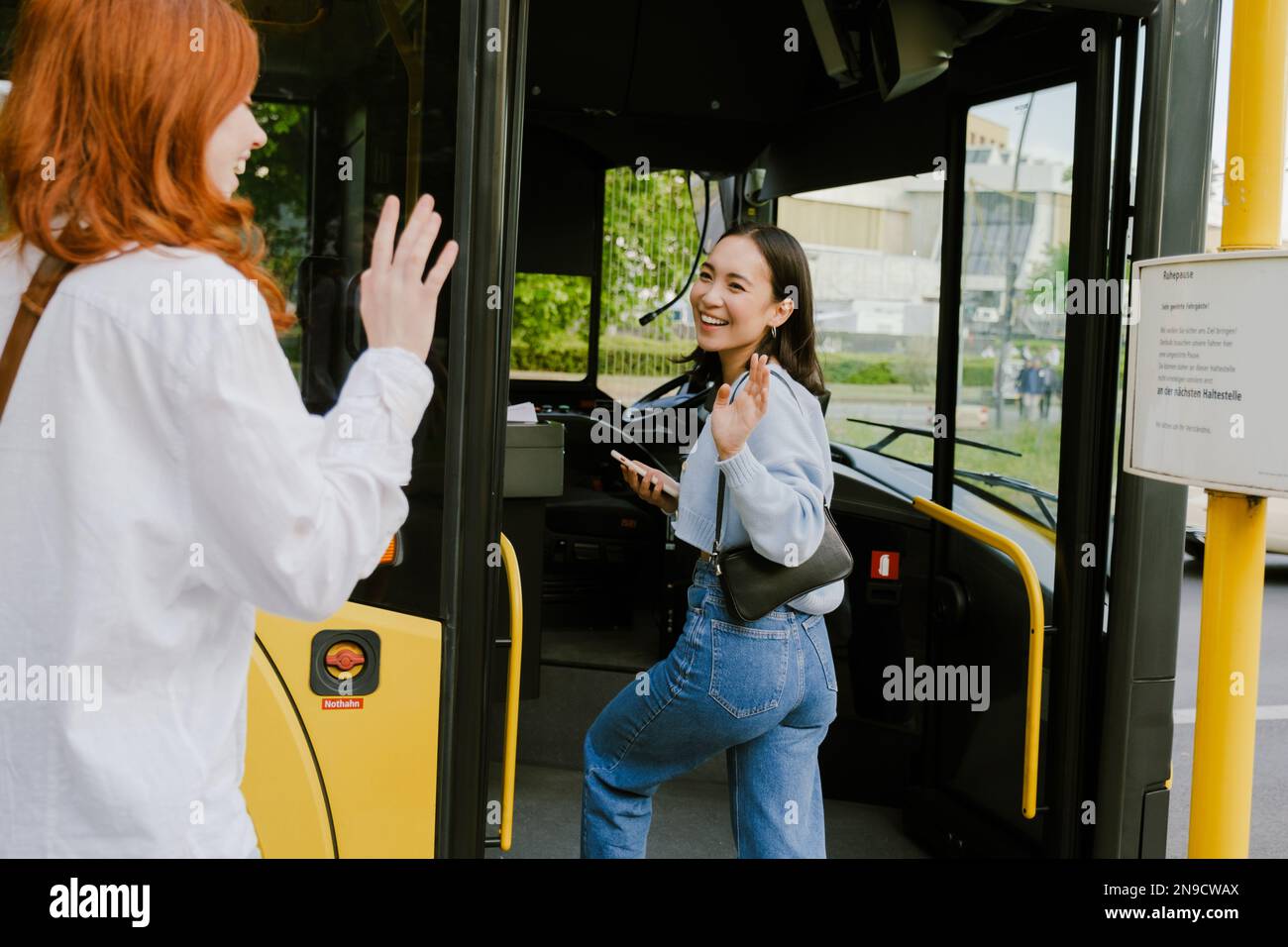 Redhead Girl Waving To Her Cute Smiling Asian Friend Who Boarding Bus And Waving To Her Too