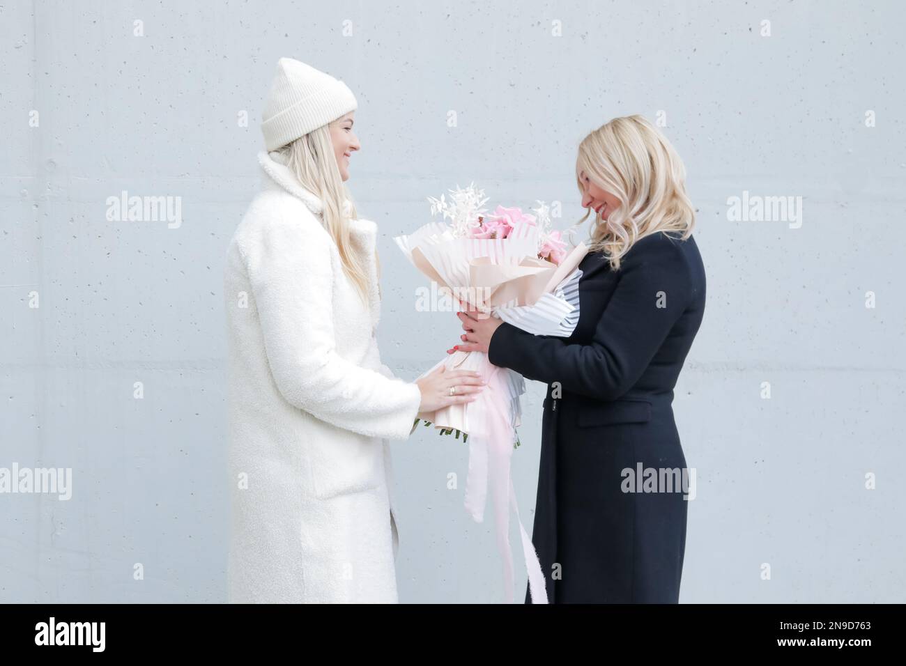 Smiling woman receiving beautiful bouquet of flowers on gray wall. Side ...