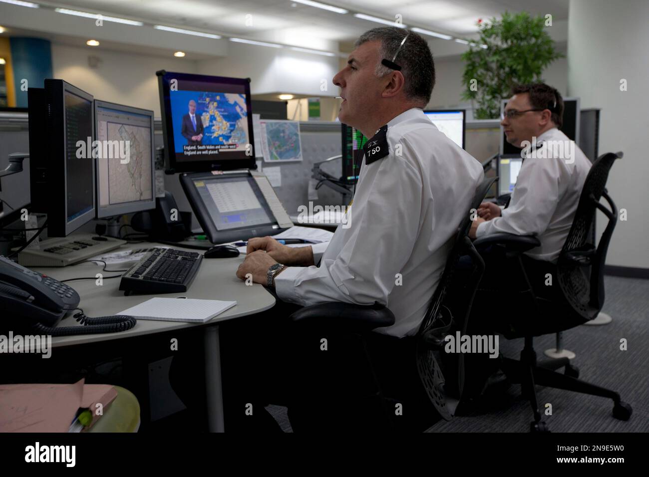Police officers work at their desks as a television weather forecast is ...