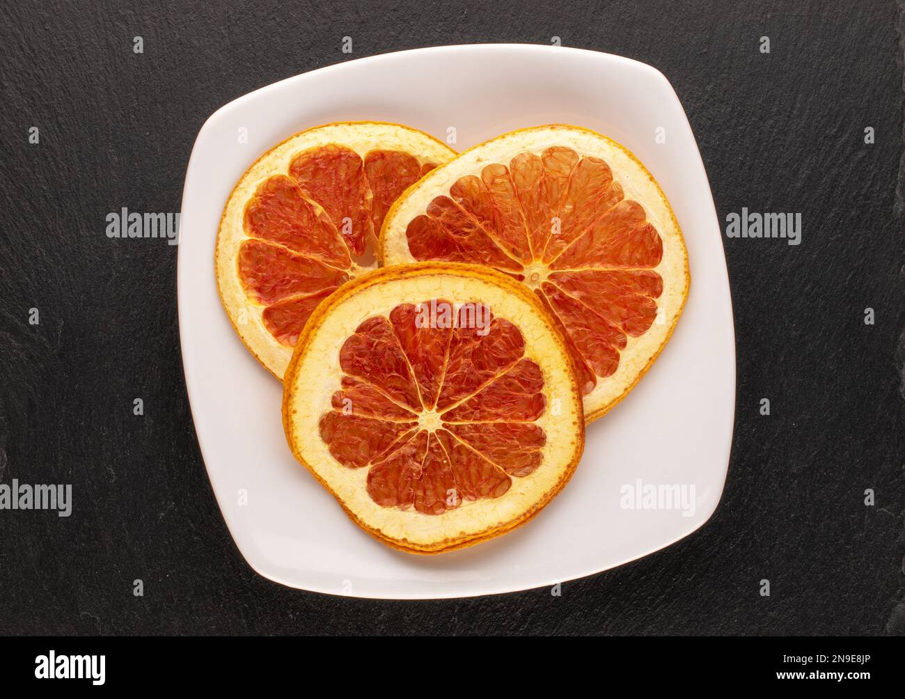 Three dry grapefruit slices with white saucer on slate stone, macro ...