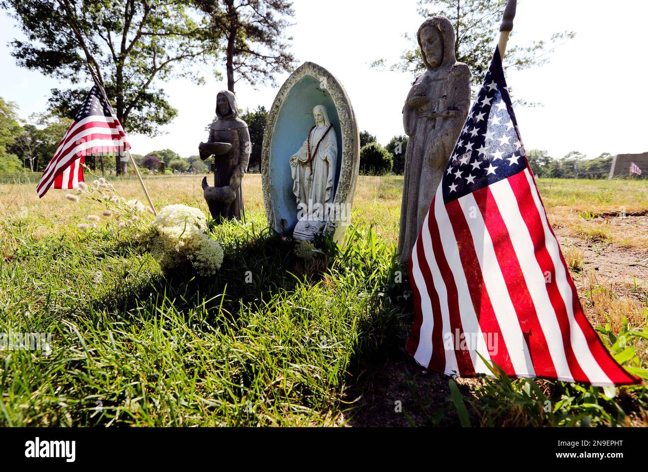 Religious statues and American flags stand at the grave site to which ...