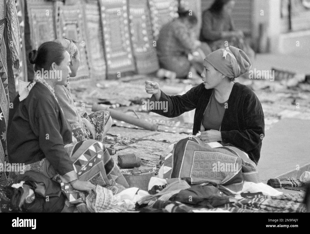 Hmong tribeswomen chat as they sew colorful cloths which they sell to ...
