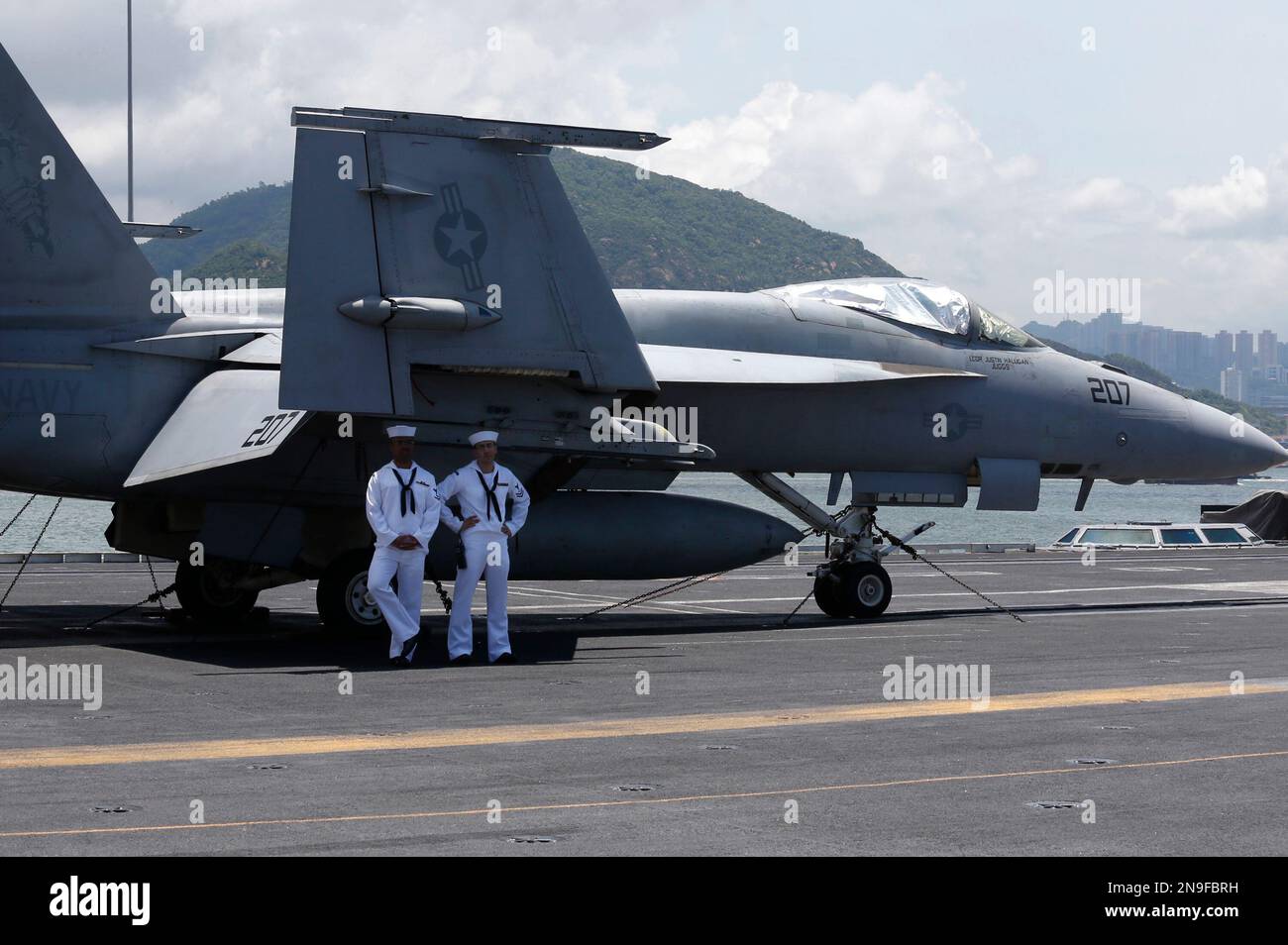 Two U.S. Navy sailors stand under the wings of an F/A-18 fighter jet on ...