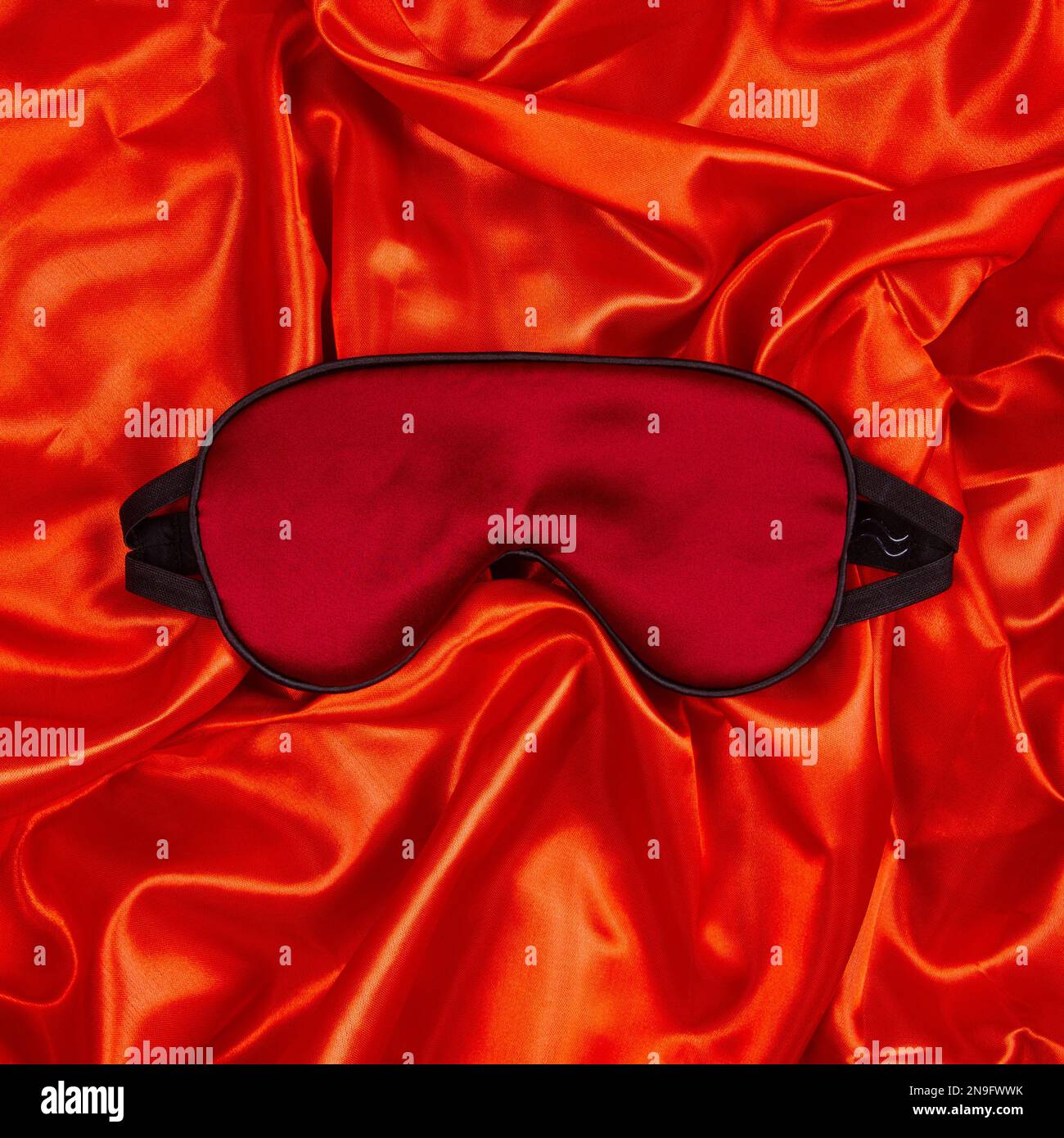 Dark red silk sleep mask lie on bright red silken background. Top view ...