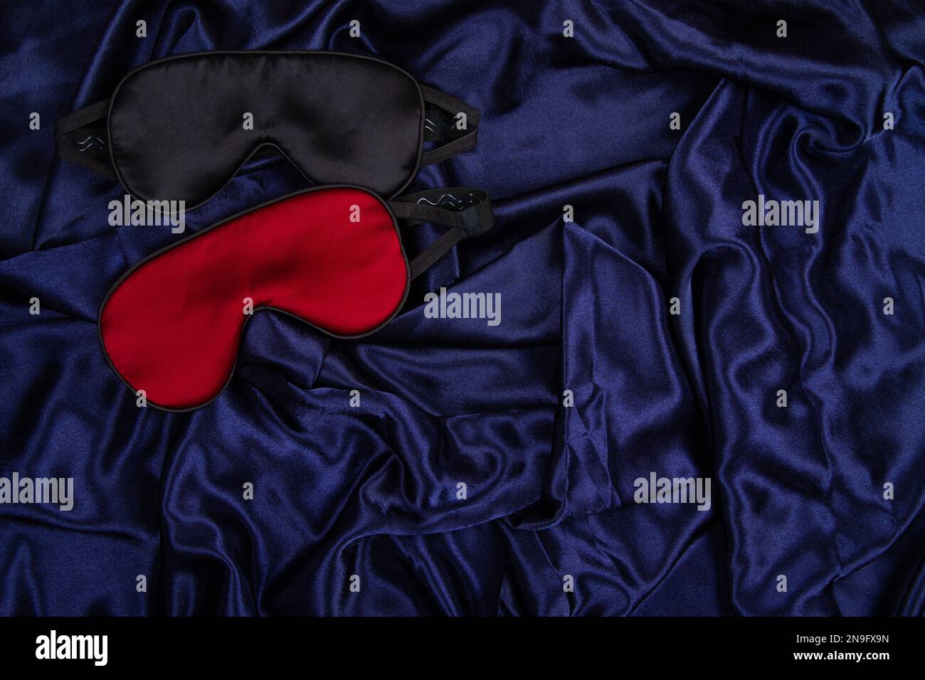 Two silk sleep mask lie on dark blue silken background. Horizontal ...