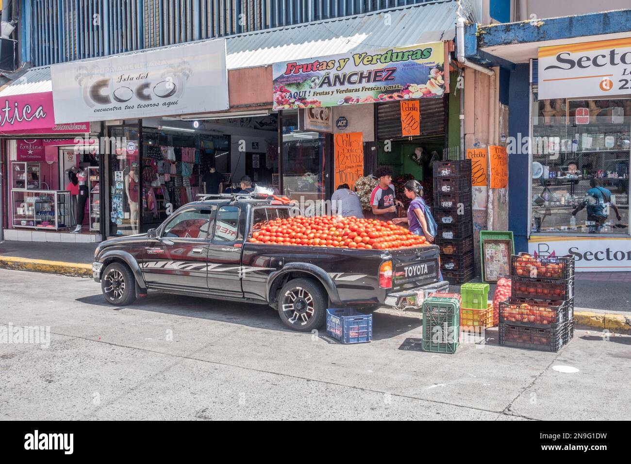 A delivery pickup truck filled with tomatoes in front of a small fruit ...