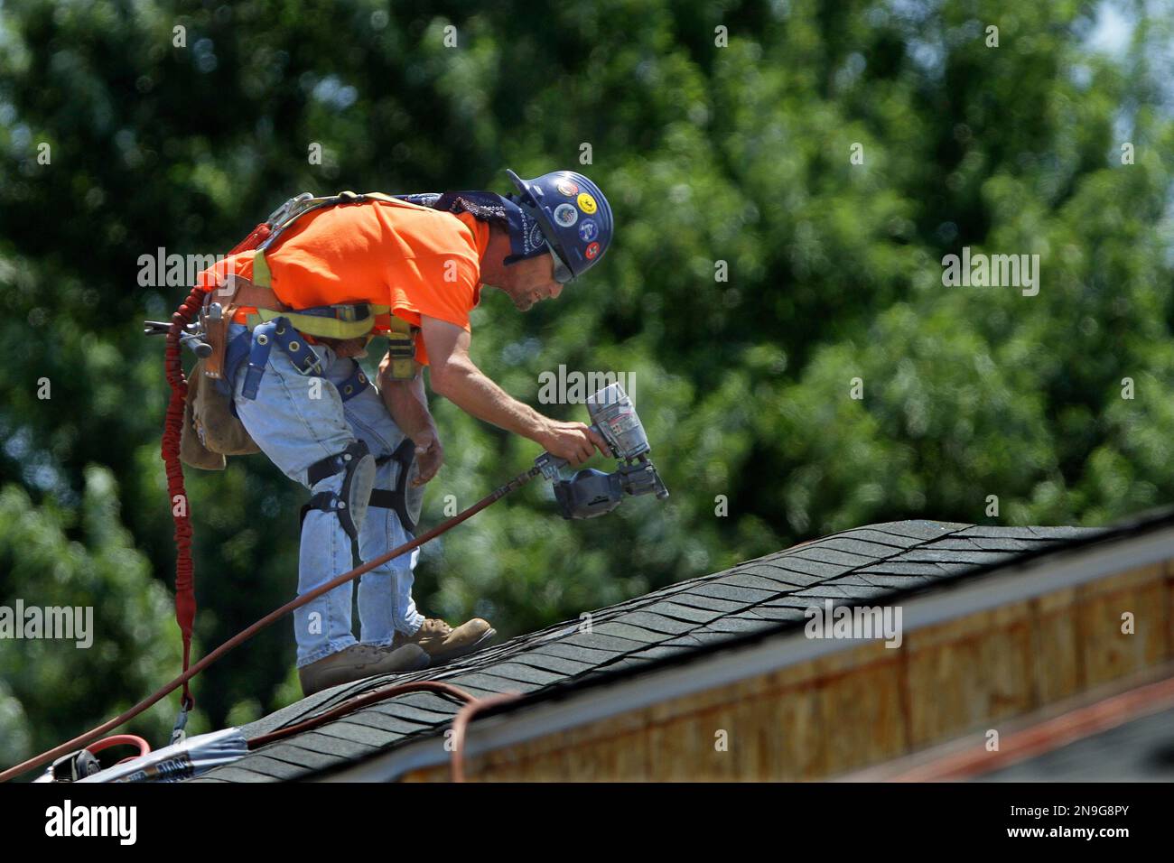 A construction worker wearing a safety harness installs roofing tiles ...