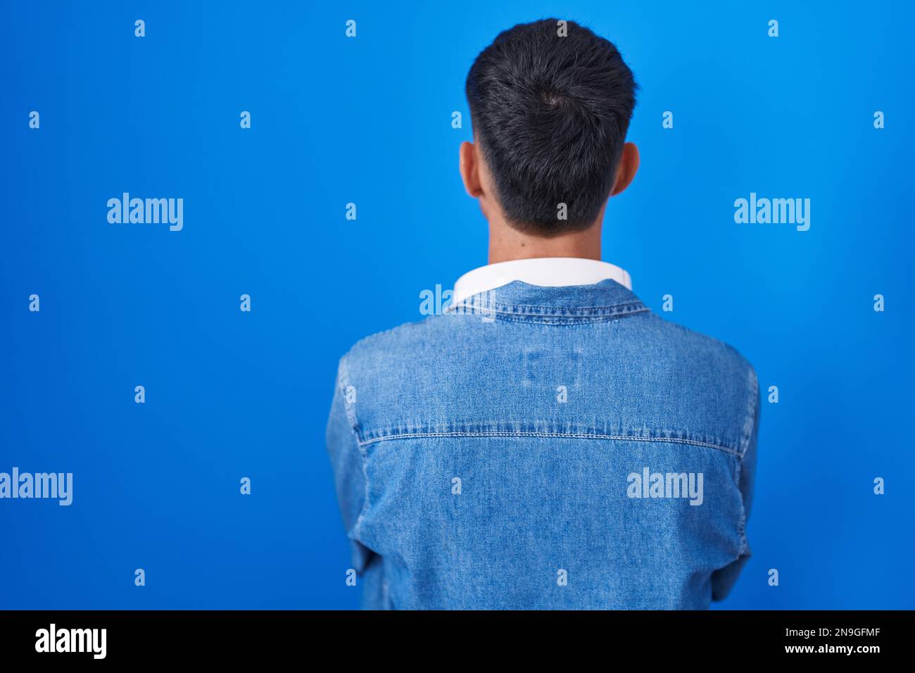 Young hispanic man standing over blue background standing backwards ...