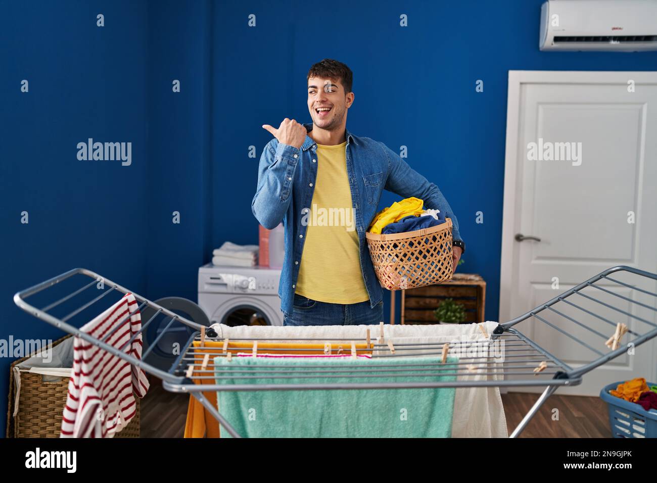 Young hispanic man hanging clothes at clothesline pointing thumb up to ...
