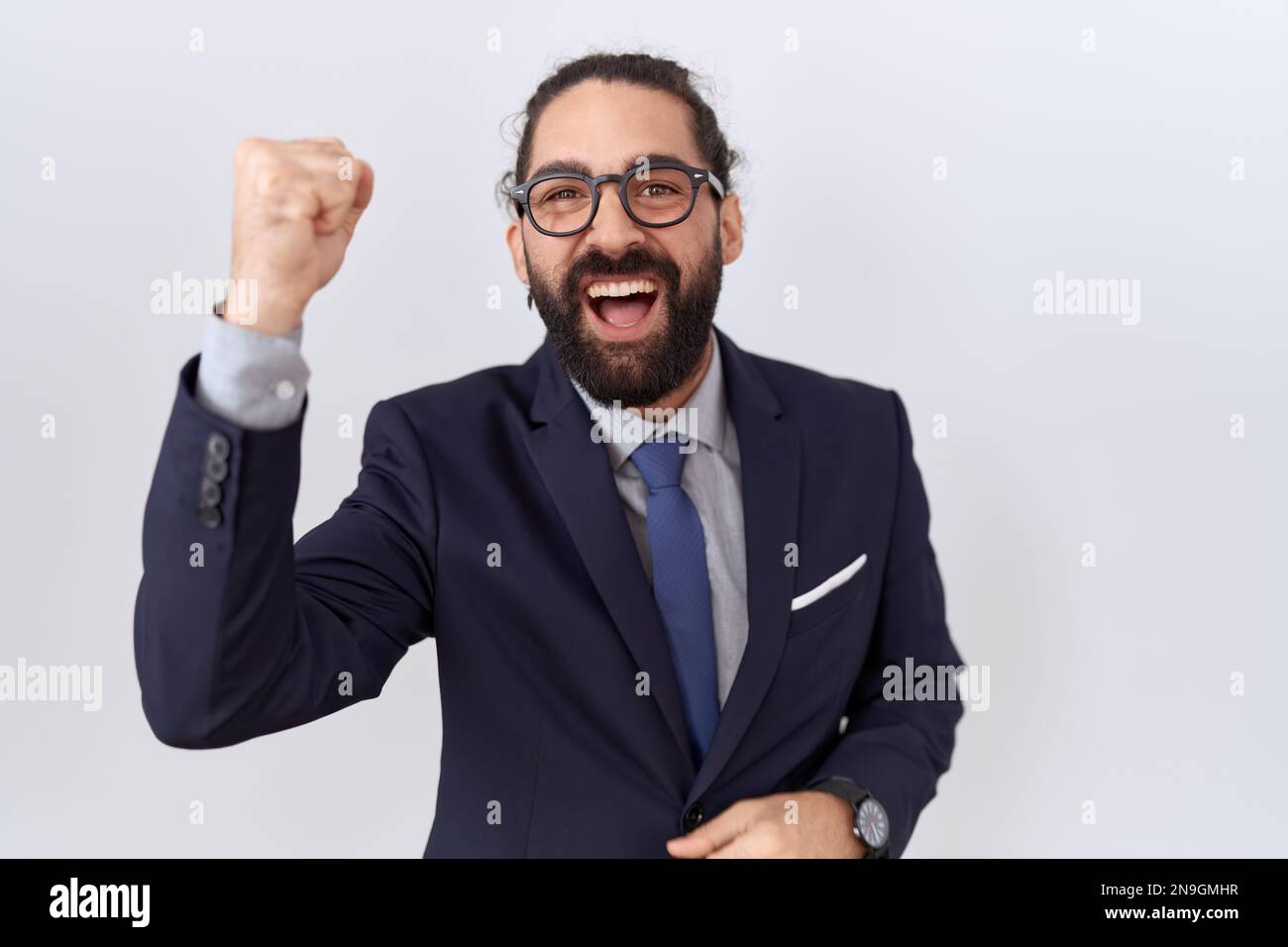 Hispanic man with beard wearing suit and tie angry and mad raising fist ...