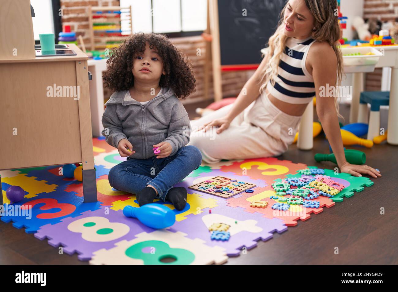 Teacher and toddler playing with maths puzzle game sitting on floor at ...