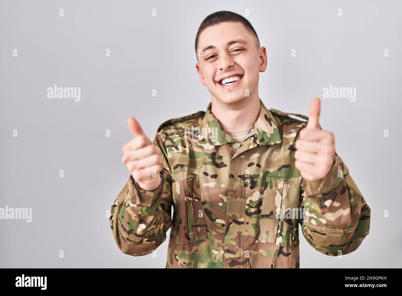 Young man wearing camouflage army uniform success sign doing positive ...