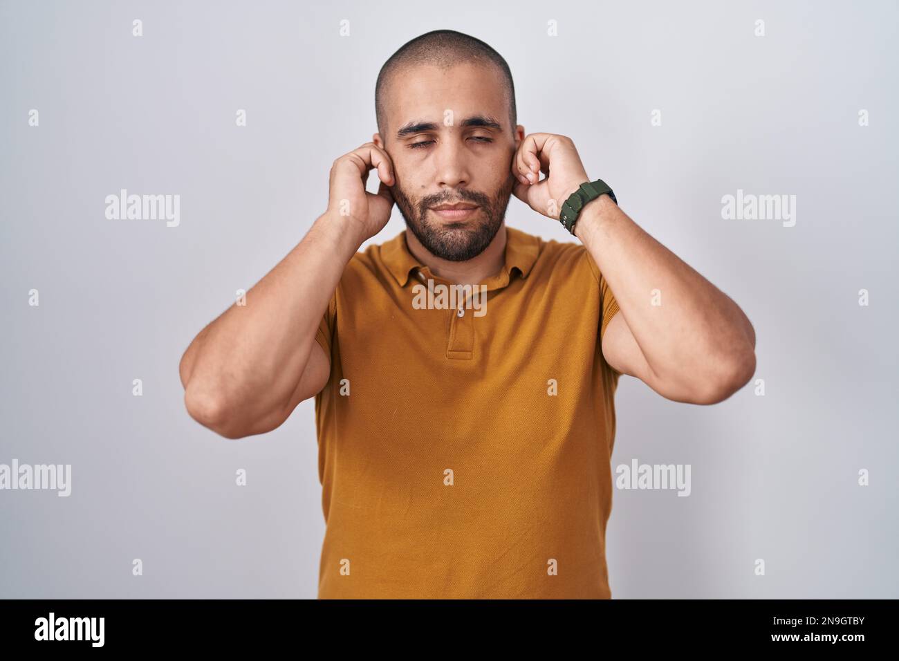 Hispanic man with beard standing over white background covering ears ...