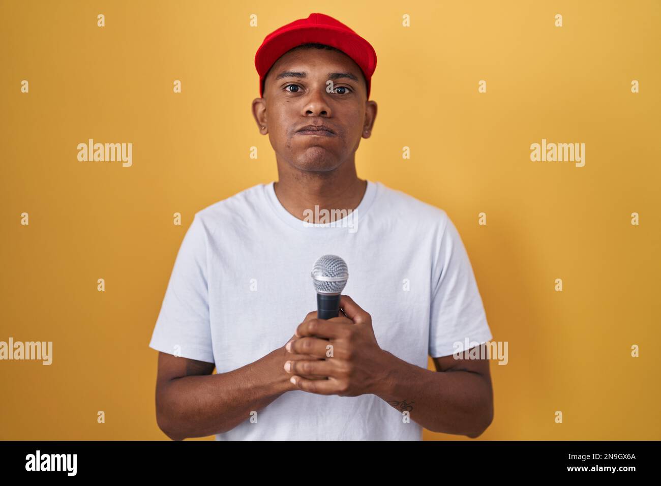 Young hispanic man singing song using microphone puffing cheeks with ...