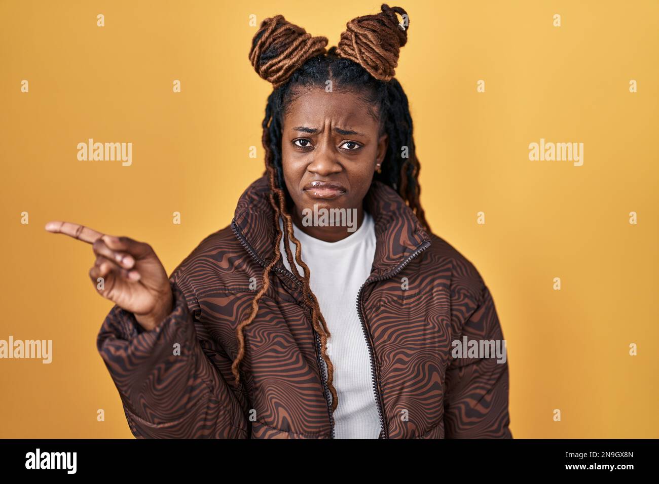 African woman with braided hair standing over yellow background ...