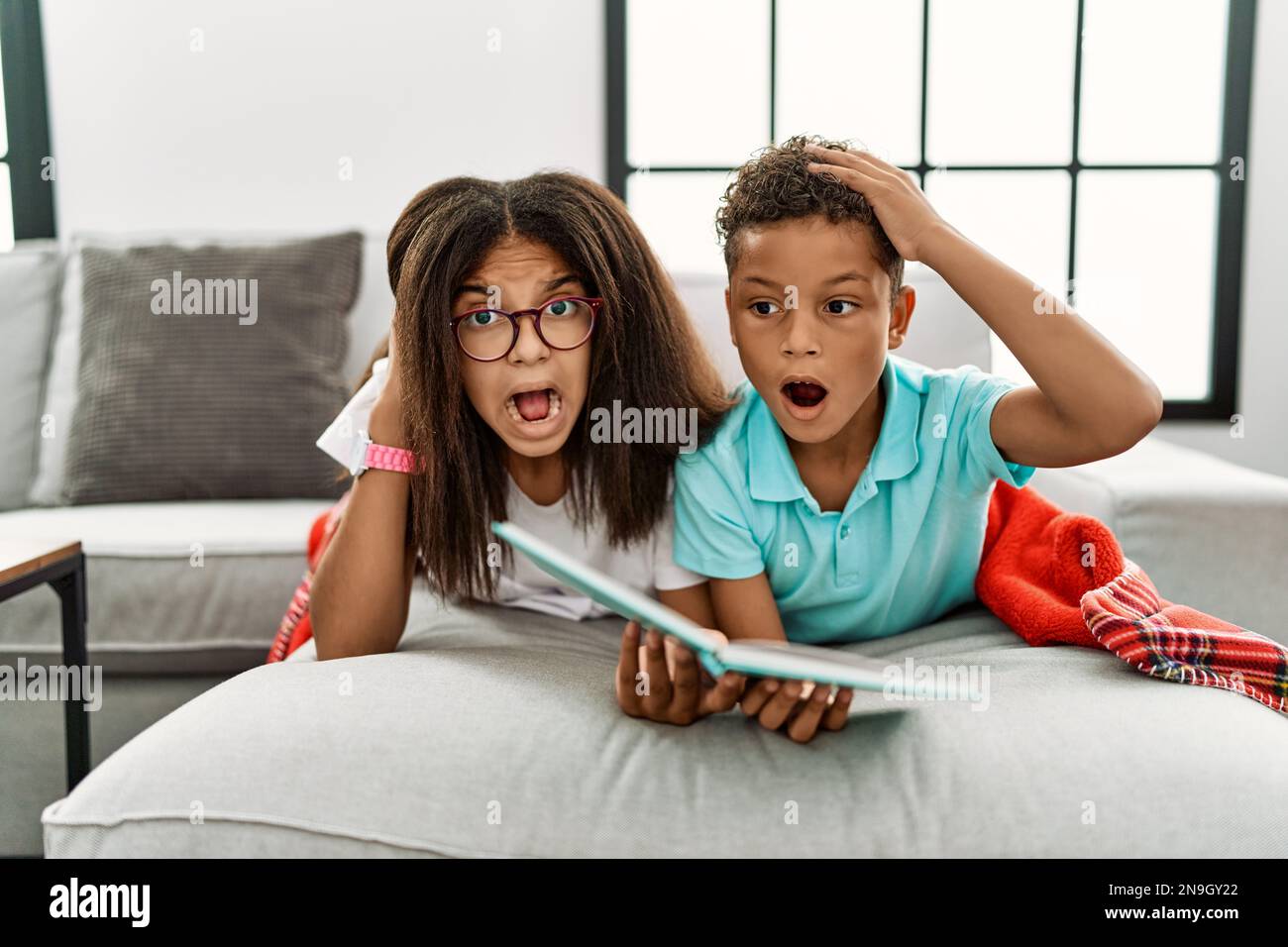 Two siblings lying on the sofa reading a book crazy and scared with ...
