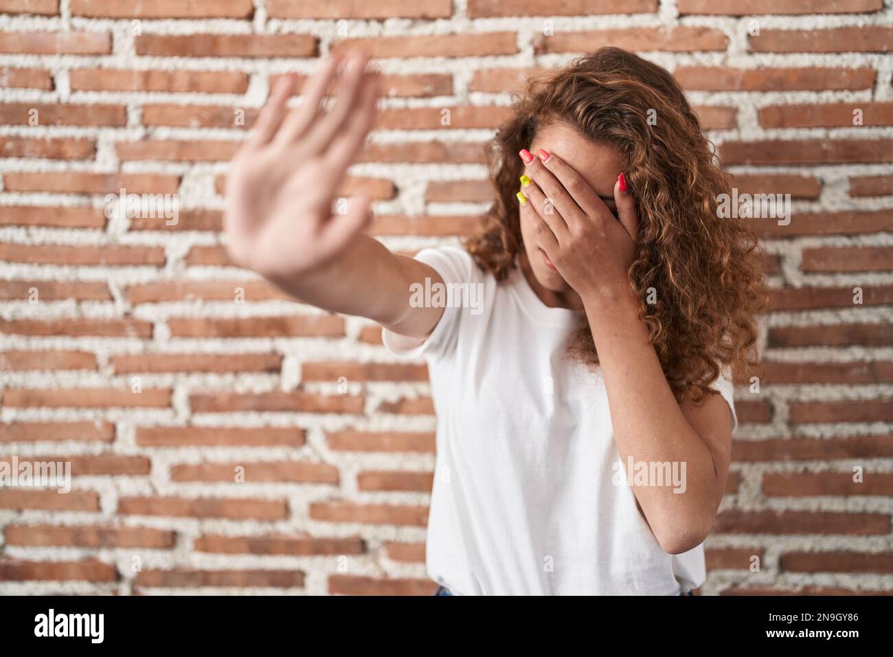 Young caucasian woman standing over bricks wall background covering ...