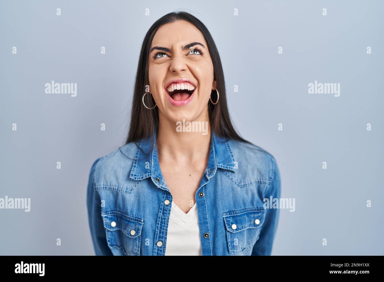 Hispanic woman standing over blue background angry and mad screaming ...
