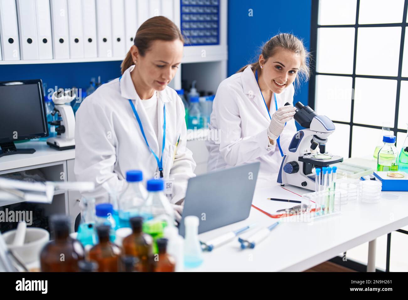 Two women scientists using microscope and laptop at laboratory Stock ...