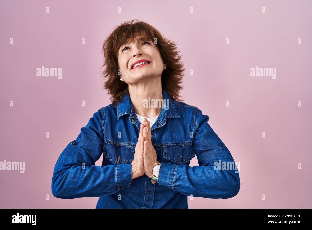 Middle age woman standing over pink background begging and praying with ...