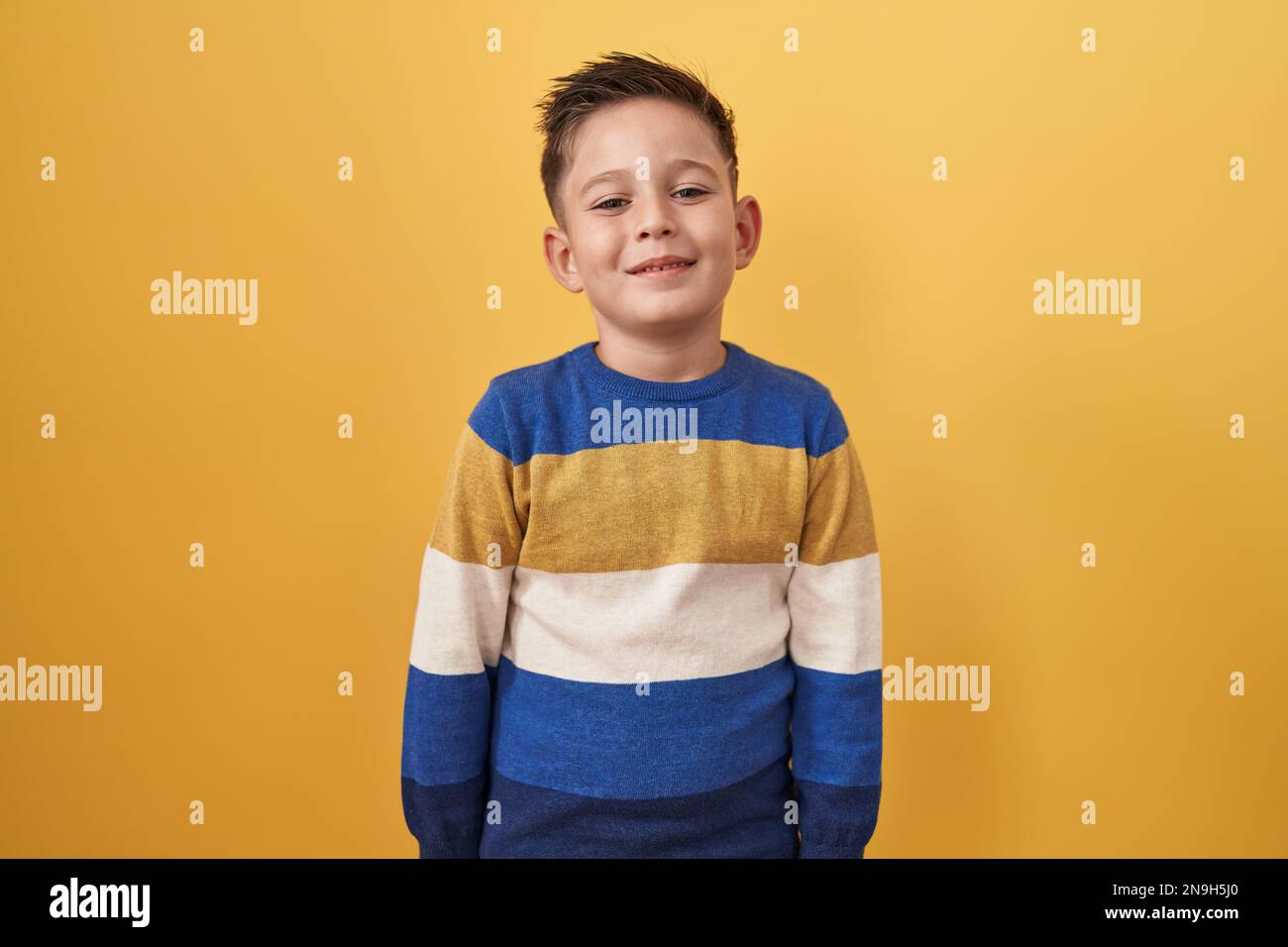 Little hispanic boy standing over yellow background with a happy and ...