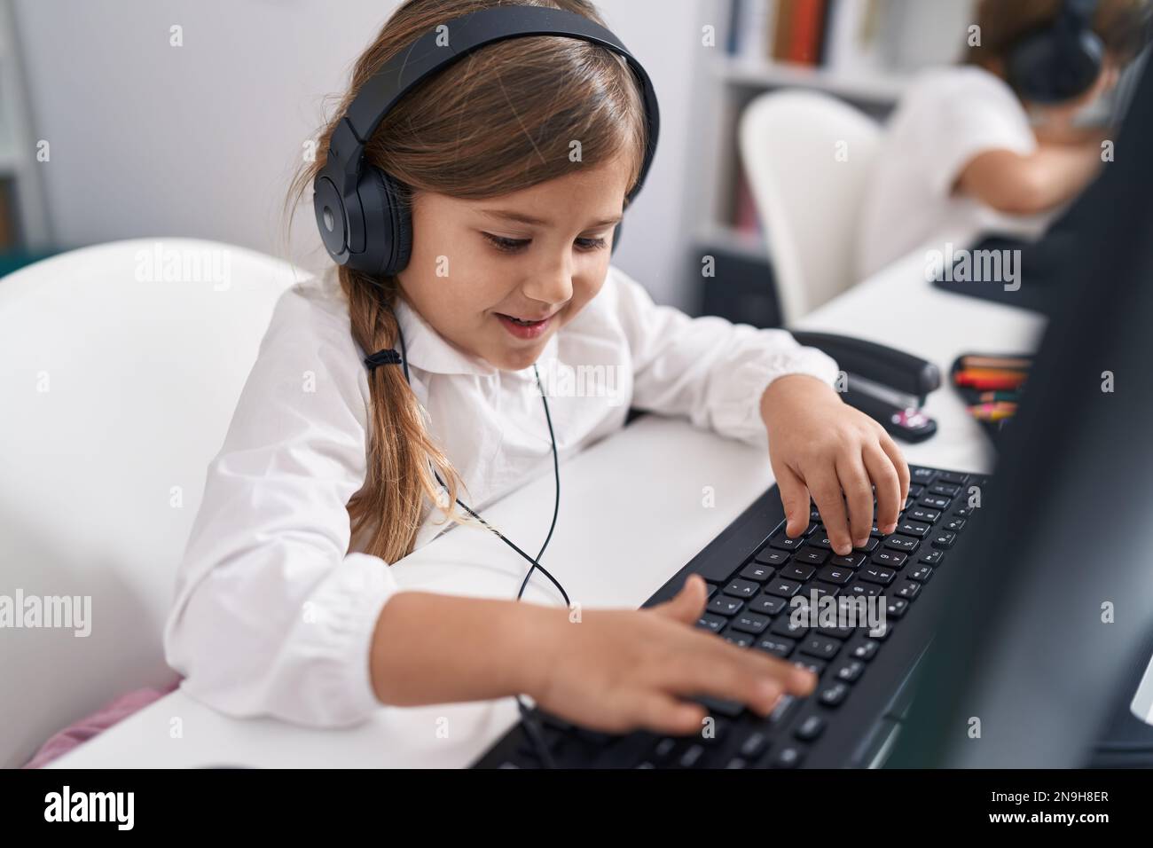 Adorable blonde girl student using computer sitting on table at ...